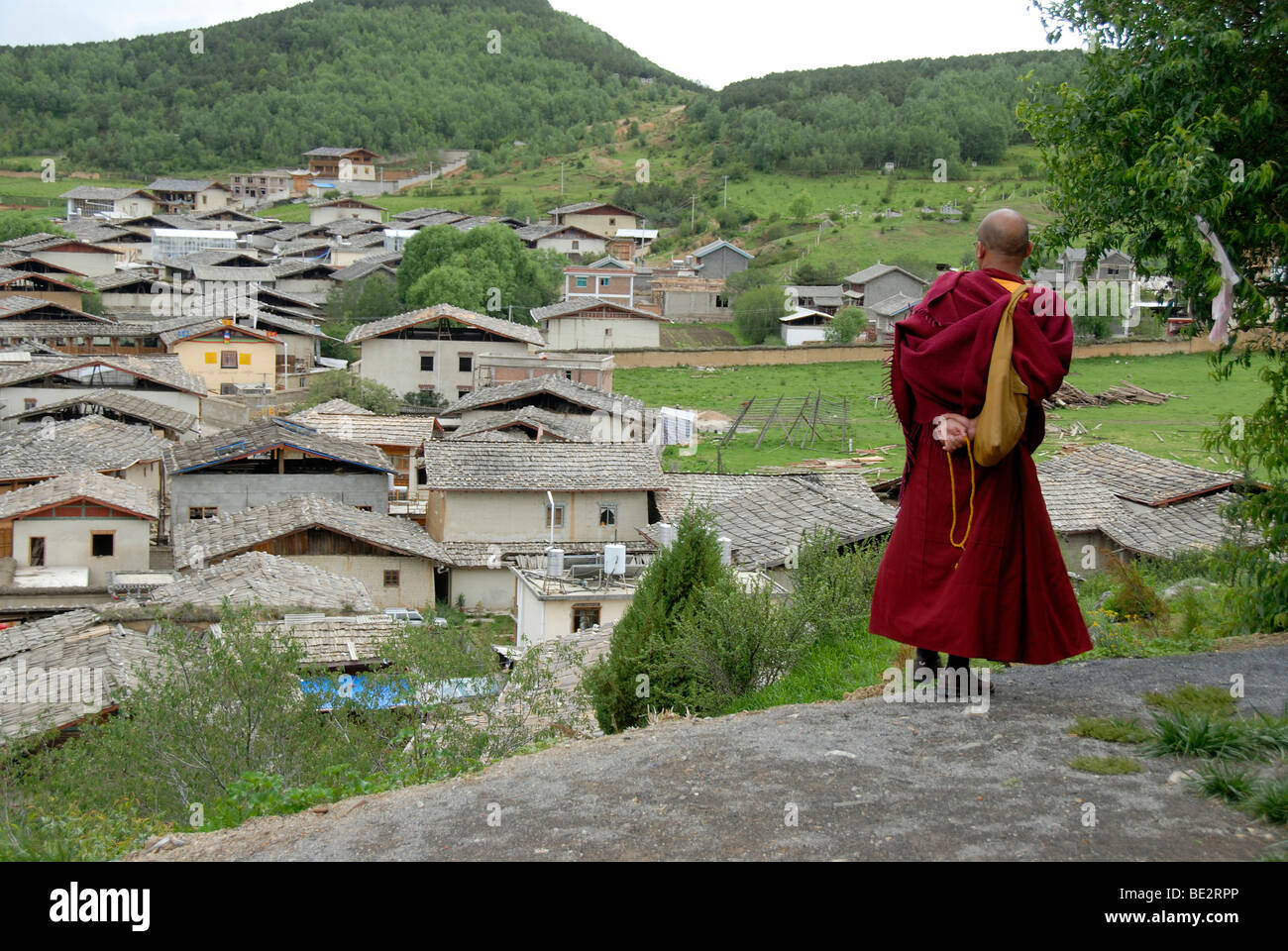 Tibetan Buddhist monk in a red robe, village with large Tibetan houses ...