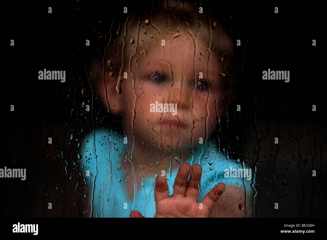 Young child looks thoughtfully from rain streaked window Stock Photo ...
