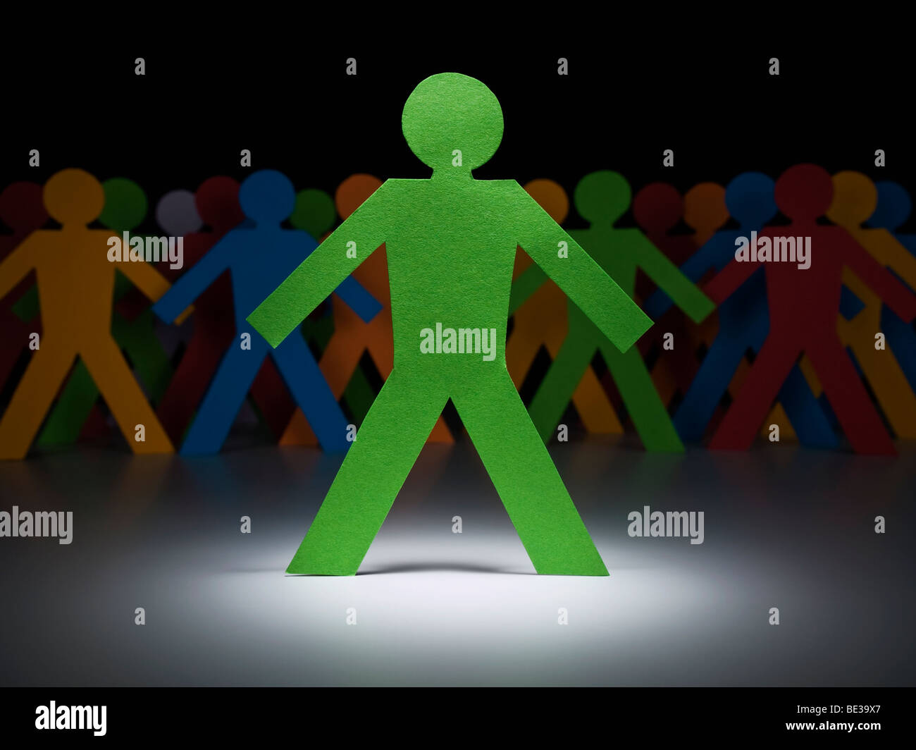 A green paper figure stands under the spotlight in front of multicolor ...