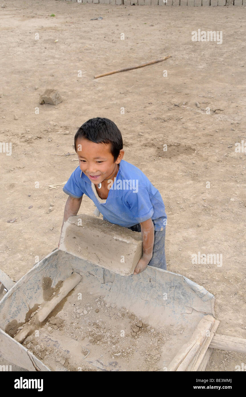 Little boy loading a wheelbarrow with bricks in a brickyard that ...