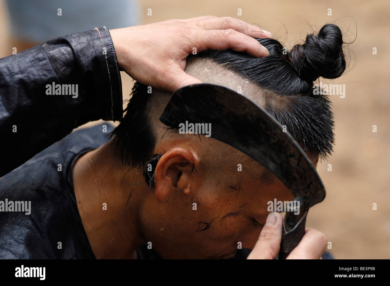 Traditional Basha hair shaving with a sickle on a man with a hair bun ...
