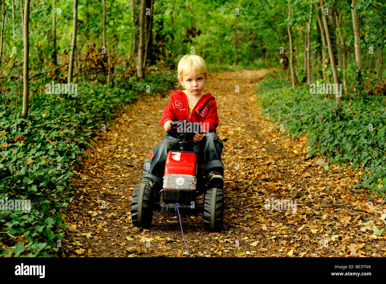 Child blond Boy driving a toy plastic tractor in woodland Stock Photo ...