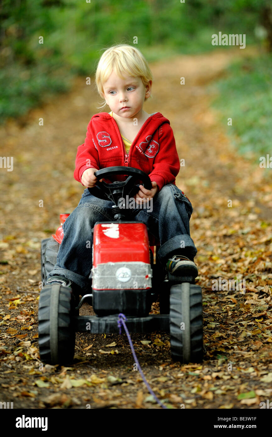 Child blond Boy driving a toy plastic tractor in woodland Stock Photo ...