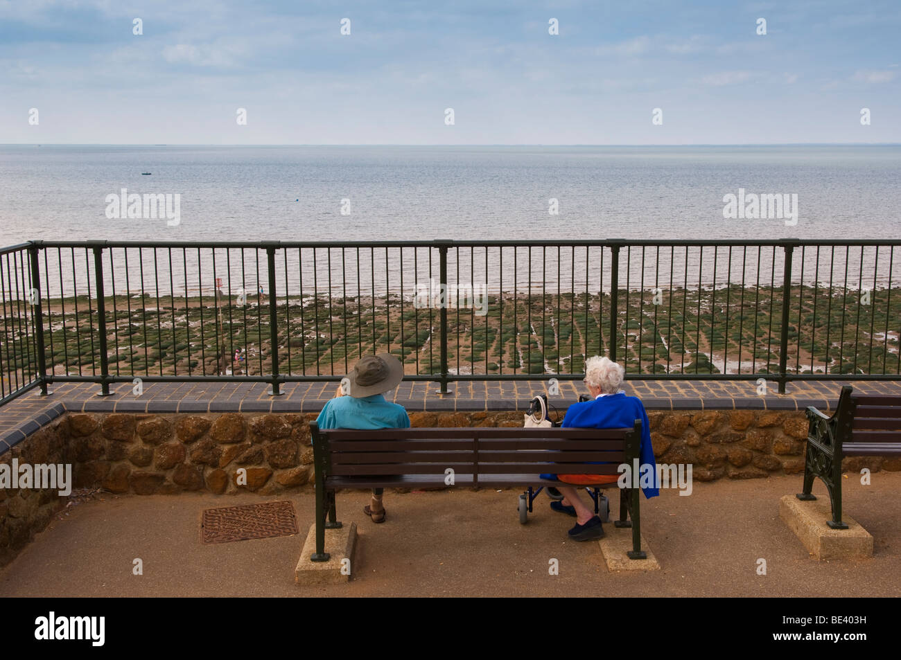 Two pensioners sitting on a seafront bench looking out to sea at ...