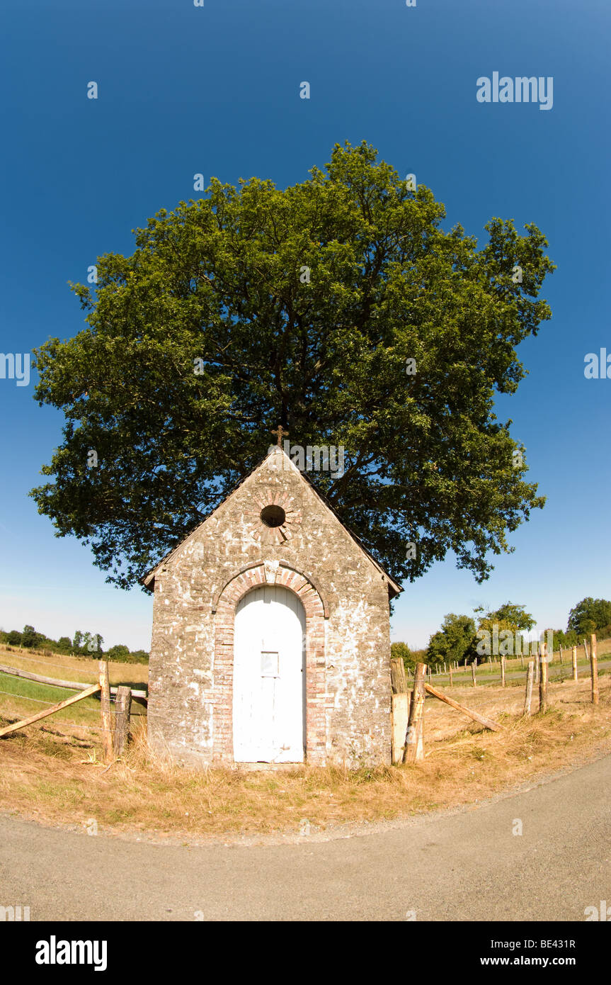 A tiny catholic chapel under a big green tree and a clear blue sky in a ...