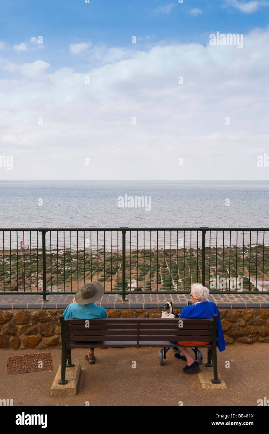 Two pensioners sitting on a seafront bench looking out to sea at ...