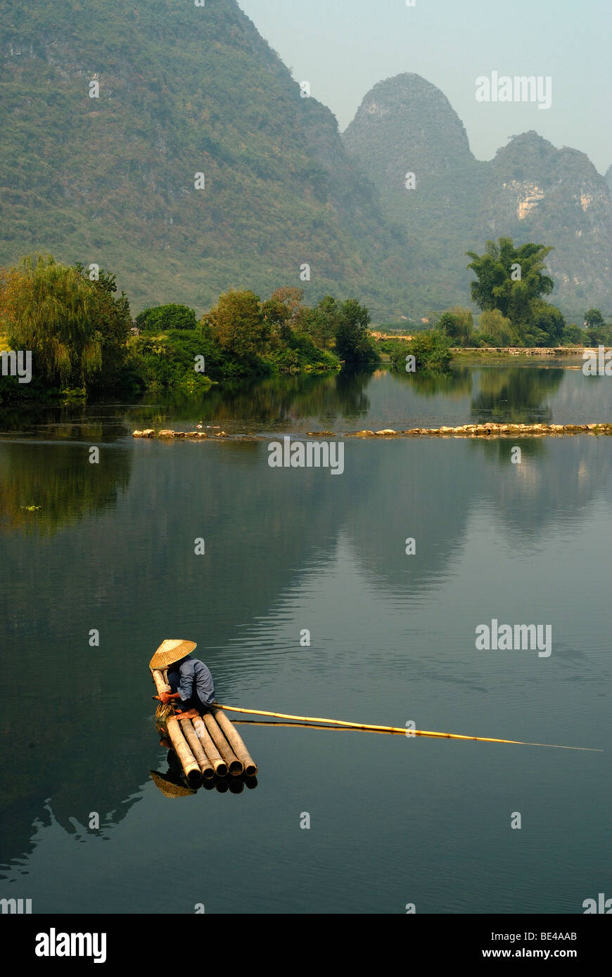 Chinese fisherman with a straw hat on a bamboo raft fishing near ...