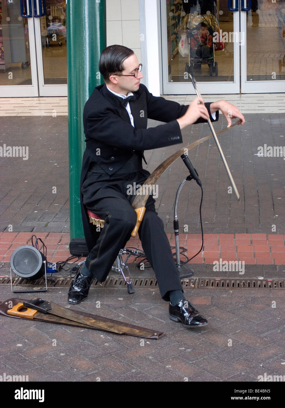 A street musician or busker in evening dress playing music by bowing a ...