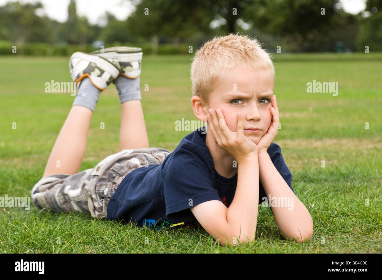 Horizontal close up portrait of a young boy scowling, lying with his ...