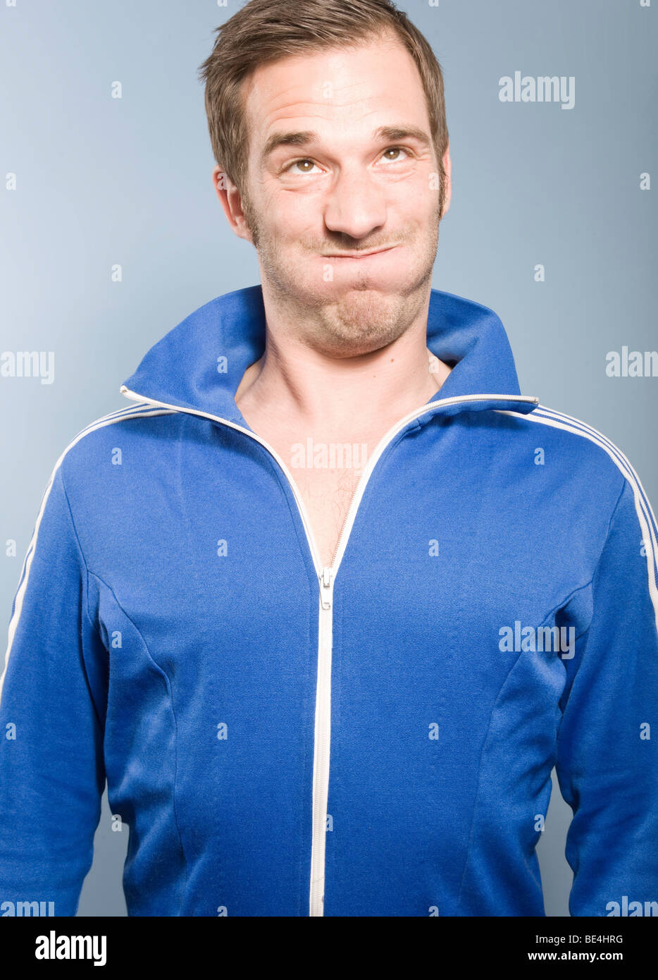 Young man posing in a retro style Adidas sport suit and blowing out his ...