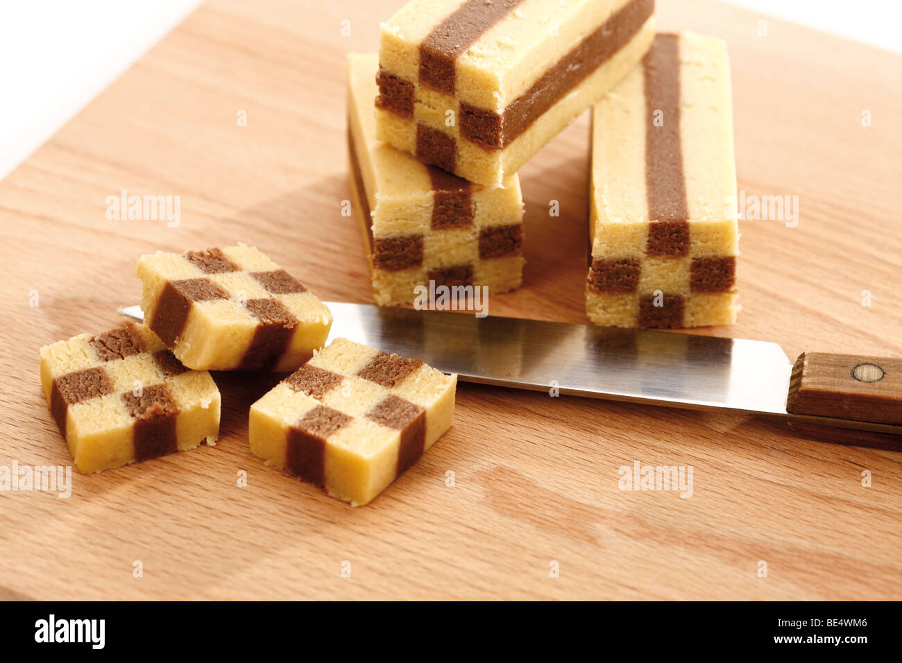 Black and white cookies, checkerboard bars on wooden board with knife ...