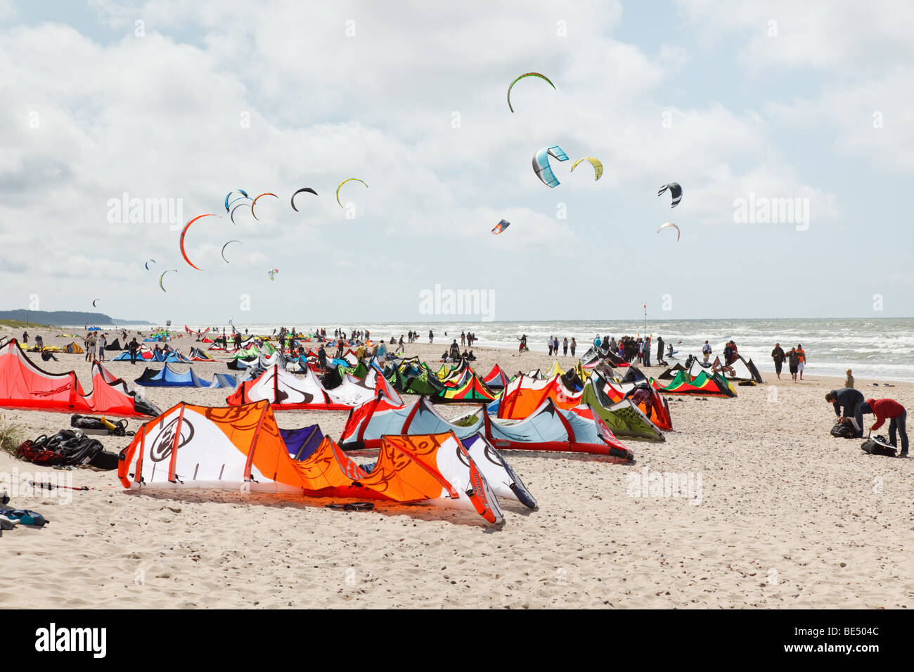 Kiteboarding competition with many active people and kites flying high ...