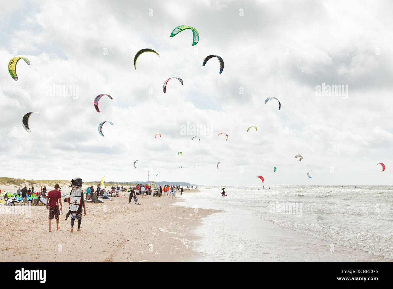Kiteboarding competition with many active people and kites flying high ...