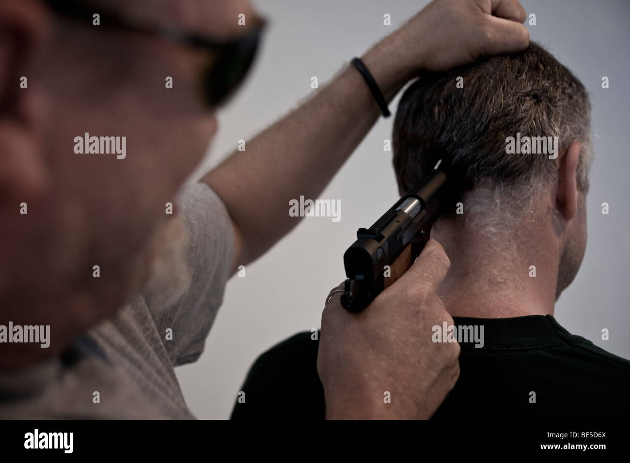 Man, disguised with sunglasses, holding another man a gun to the back ...