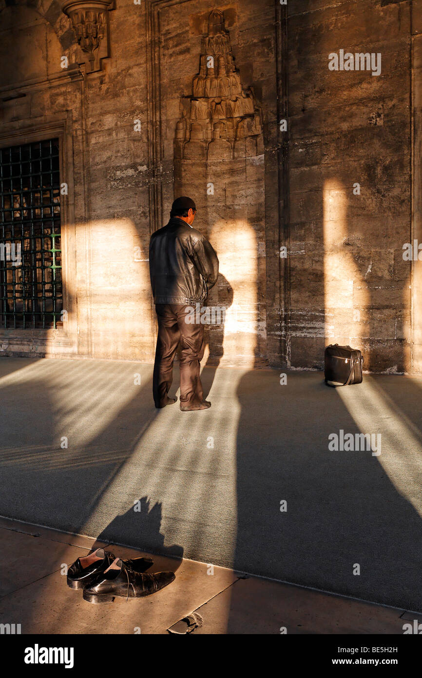 Muslim man praying in front of a prayer niche, shoes taken off, Iskele ...