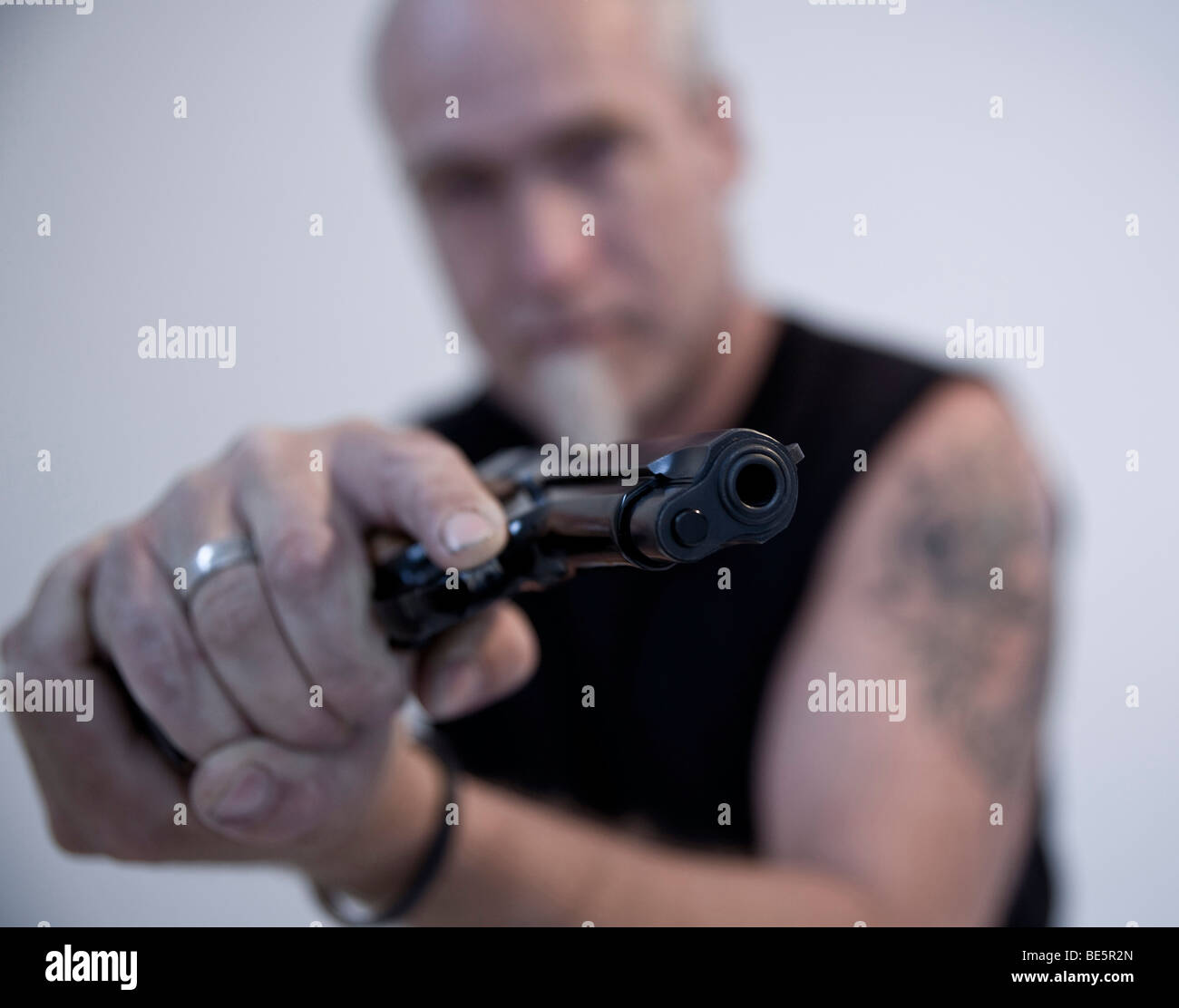 Man with a pointed beard and a tattoo on the upper arm, holding a gun ...