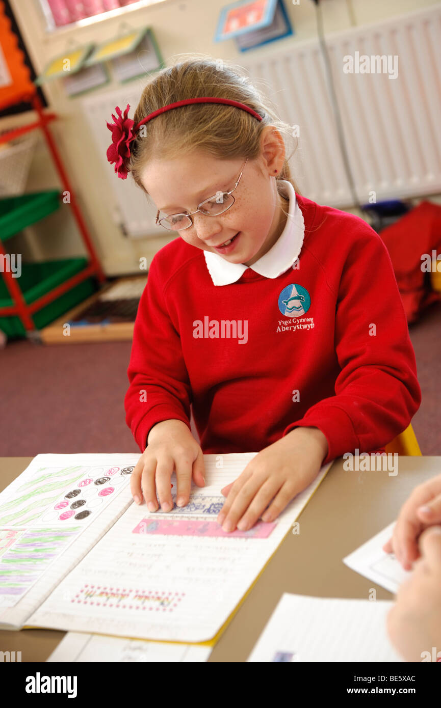 Young child reading from her exercise course book in a Welsh language ...
