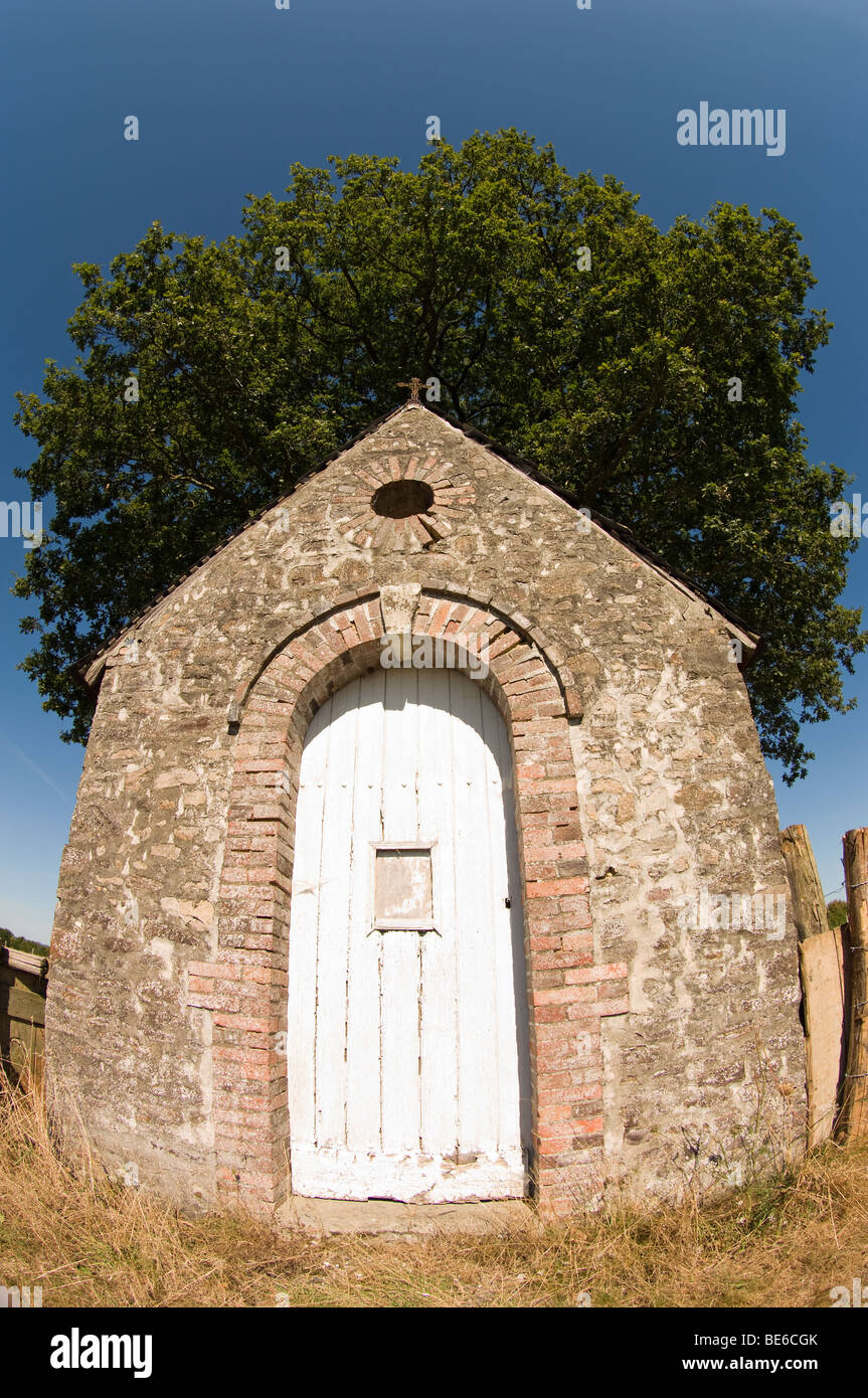 A tiny catholic chapel under a green tree in a small French village. A ...