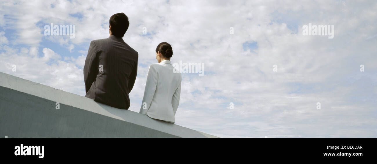Businessman and businesswoman sitting side by side on rooftop ledge ...