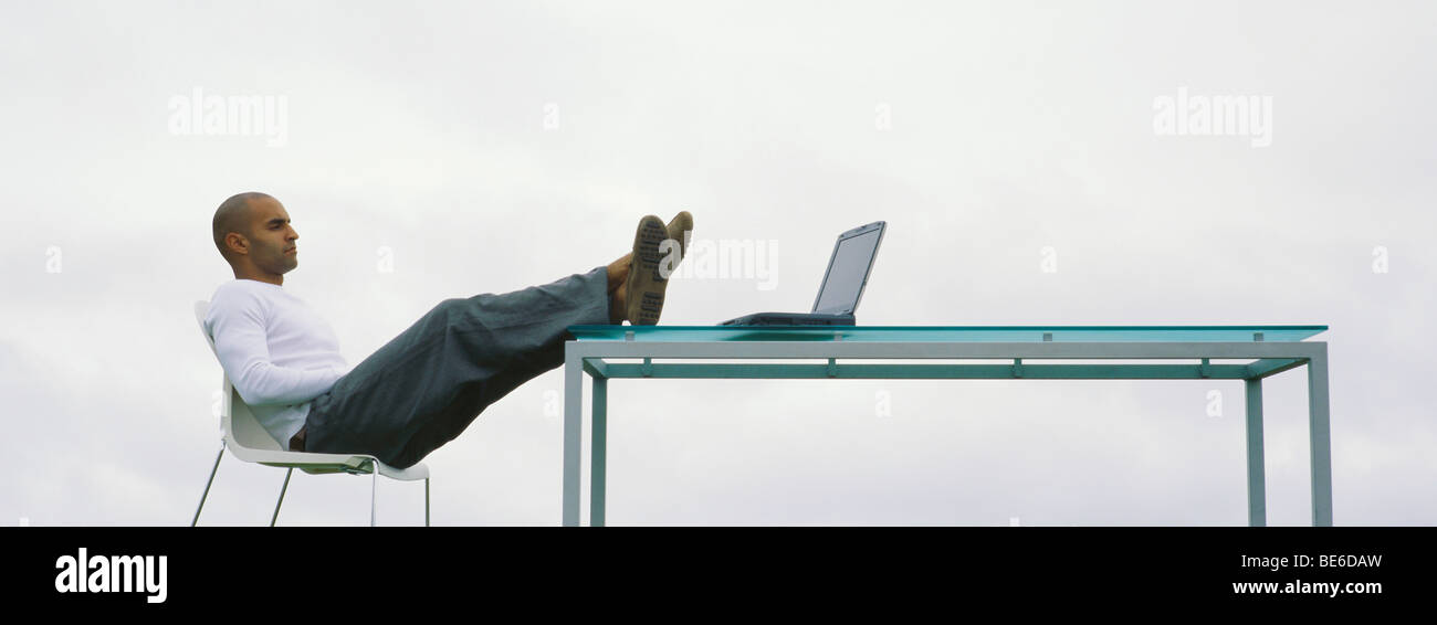 Man sitting outdoors with feet up on table, looking at laptop computer ...