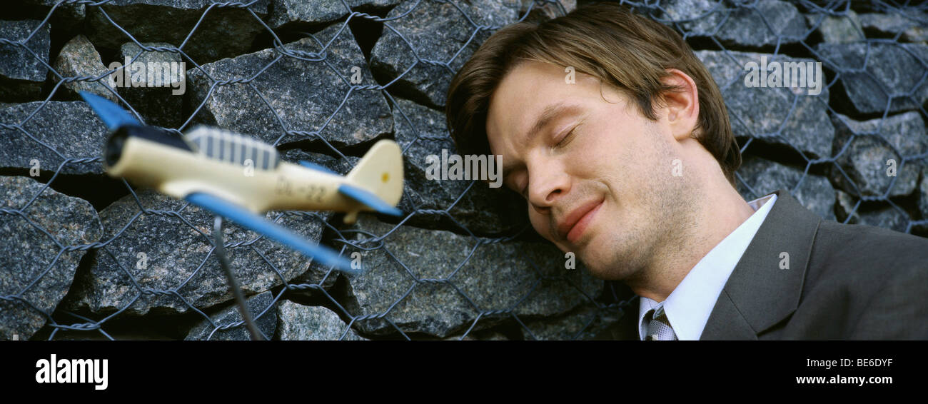 Man with eyes closed, smiling, leaning head against wall, toy airplane ...