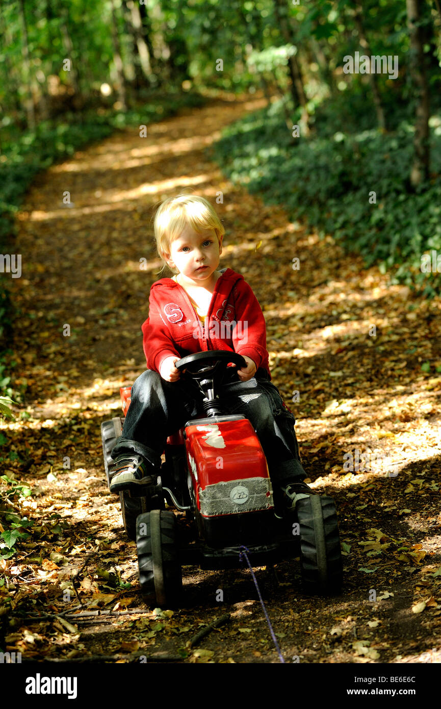 Child blond Boy driving a toy plastic tractor in woodland Stock Photo ...