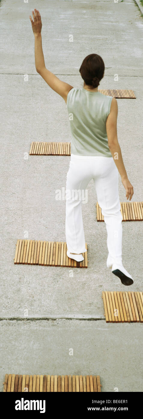 Woman hopping from one stepping stone to another, rear view Stock Photo ...