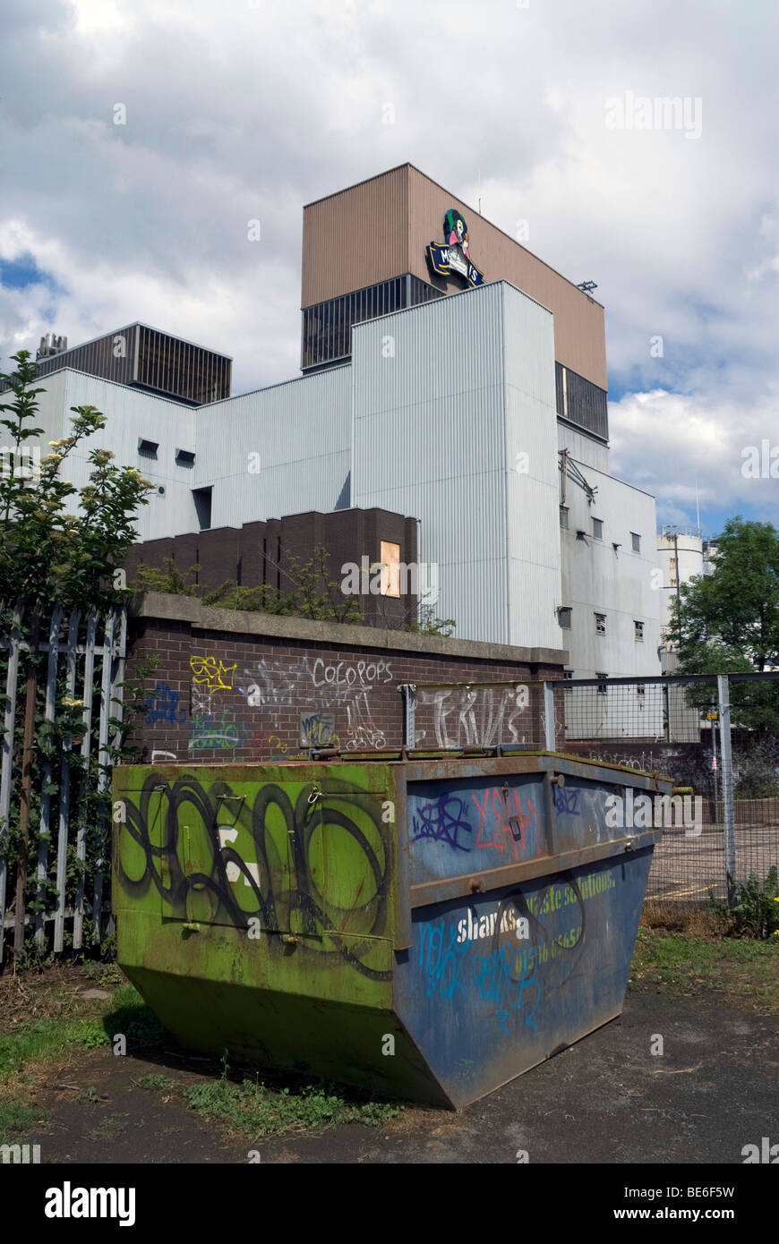 A green and blue skip with the disused brewery behind it Stock Photo ...