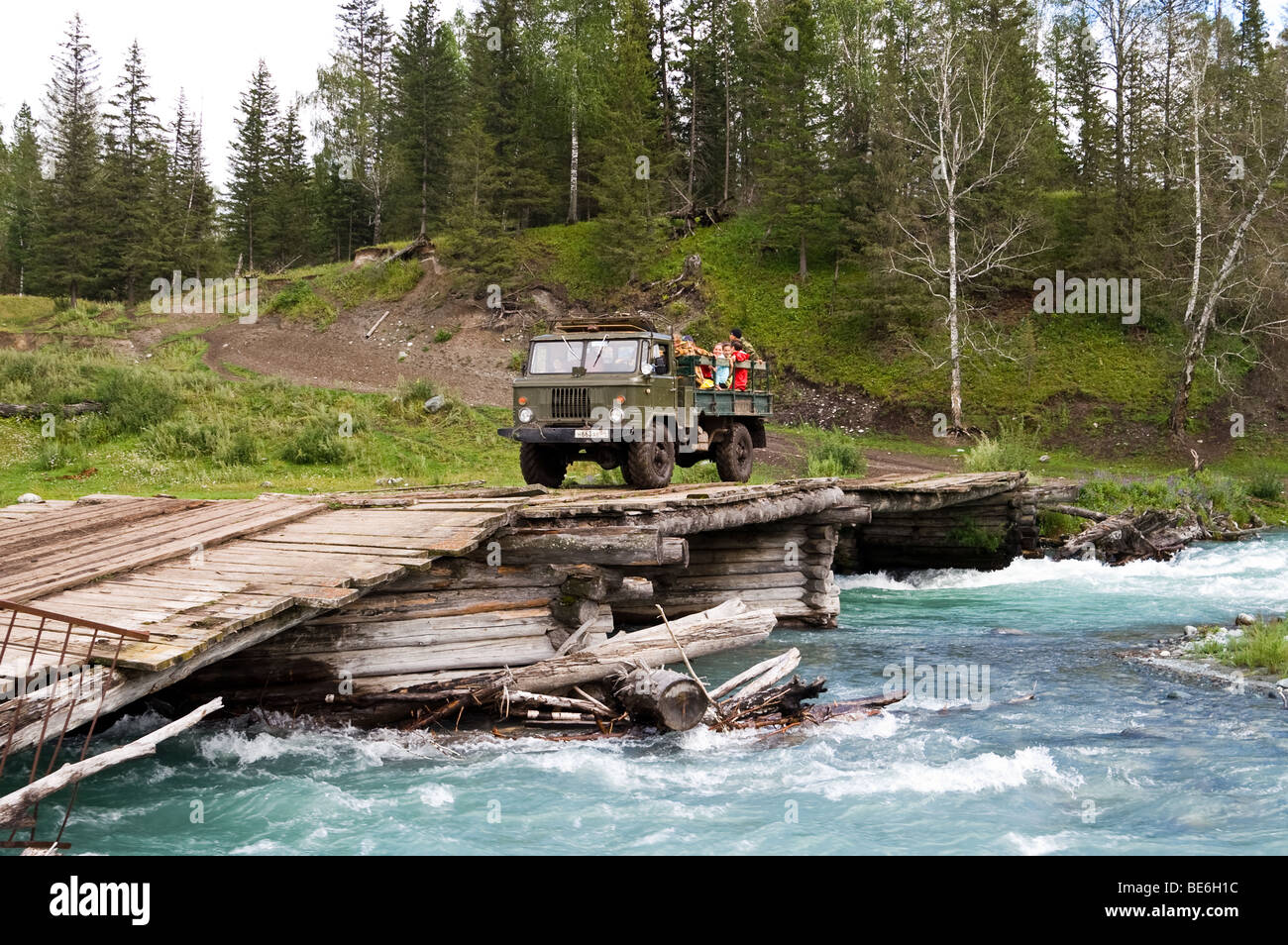 A truck with people on board crossing mountain river by a wooden bridge ...