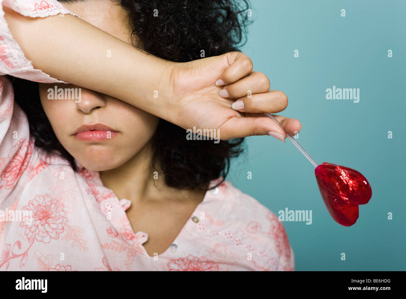 Woman frowning and covering eyes with arm, holding heart-shaped ...