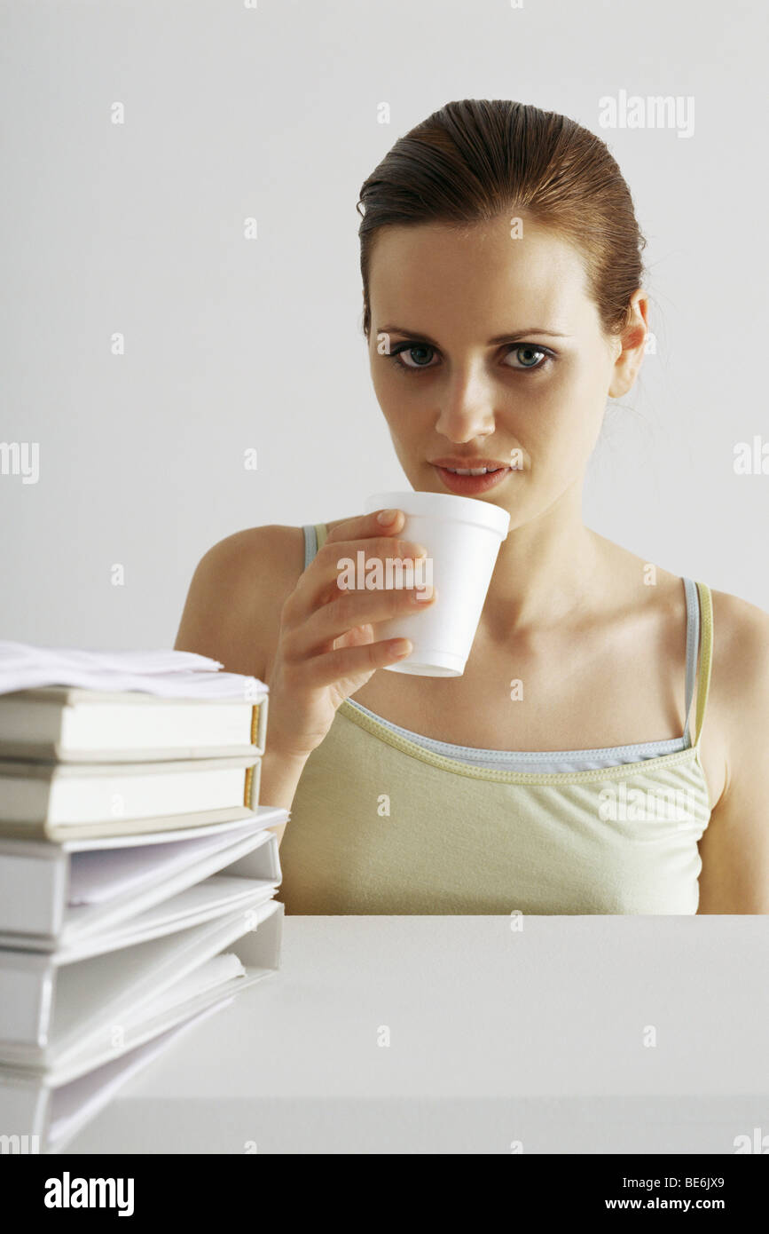Woman taking break, drinking from disposable cup, stack of binders in ...