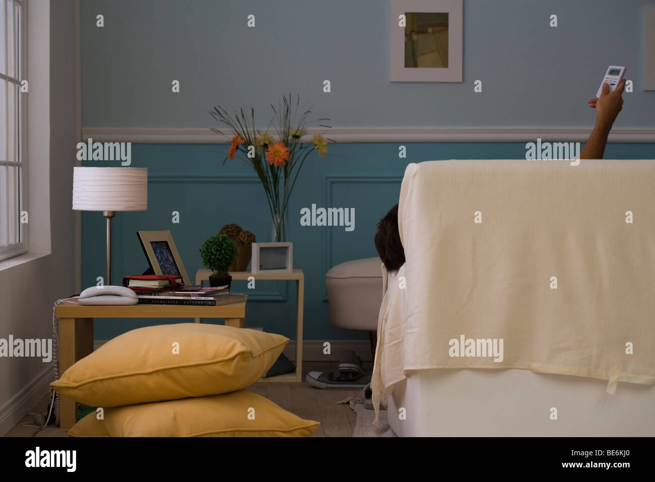 Person reclining on sofa controlling air conditioner with remote ...