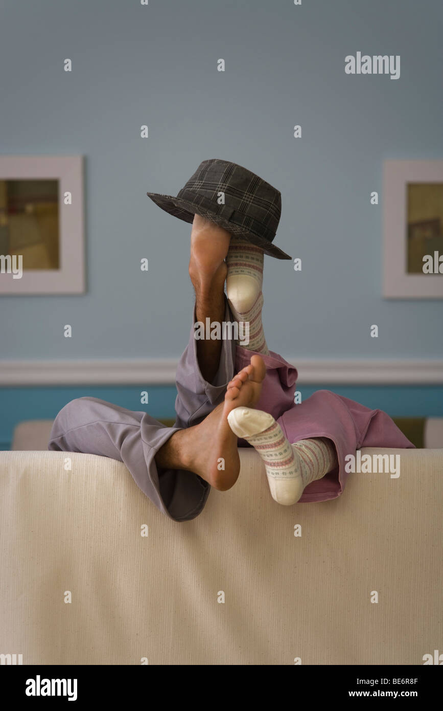 Two people reclining on sofa, legs raised together, hat set atop feet ...