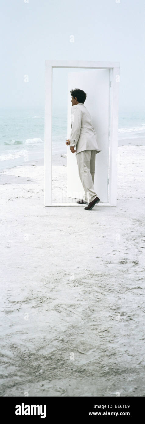 Man opening and entering door placed on beach Stock Photo - Alamy