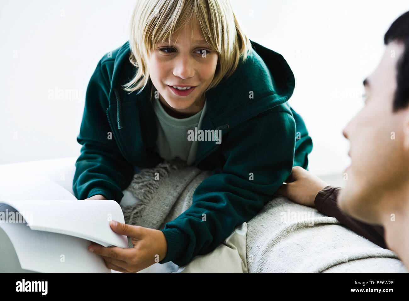 Boy leaning against sofa talking to older brother Stock Photo - Alamy