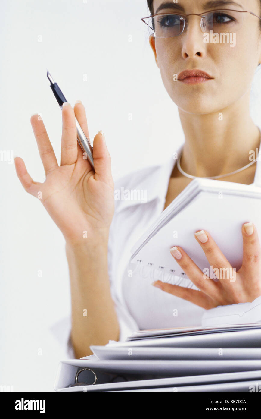 Woman holding notepad, looking away in thought, stack of binders in ...
