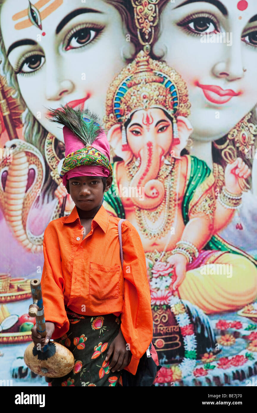 Indian beggar boy with musical instrument against a poster of hindu ...