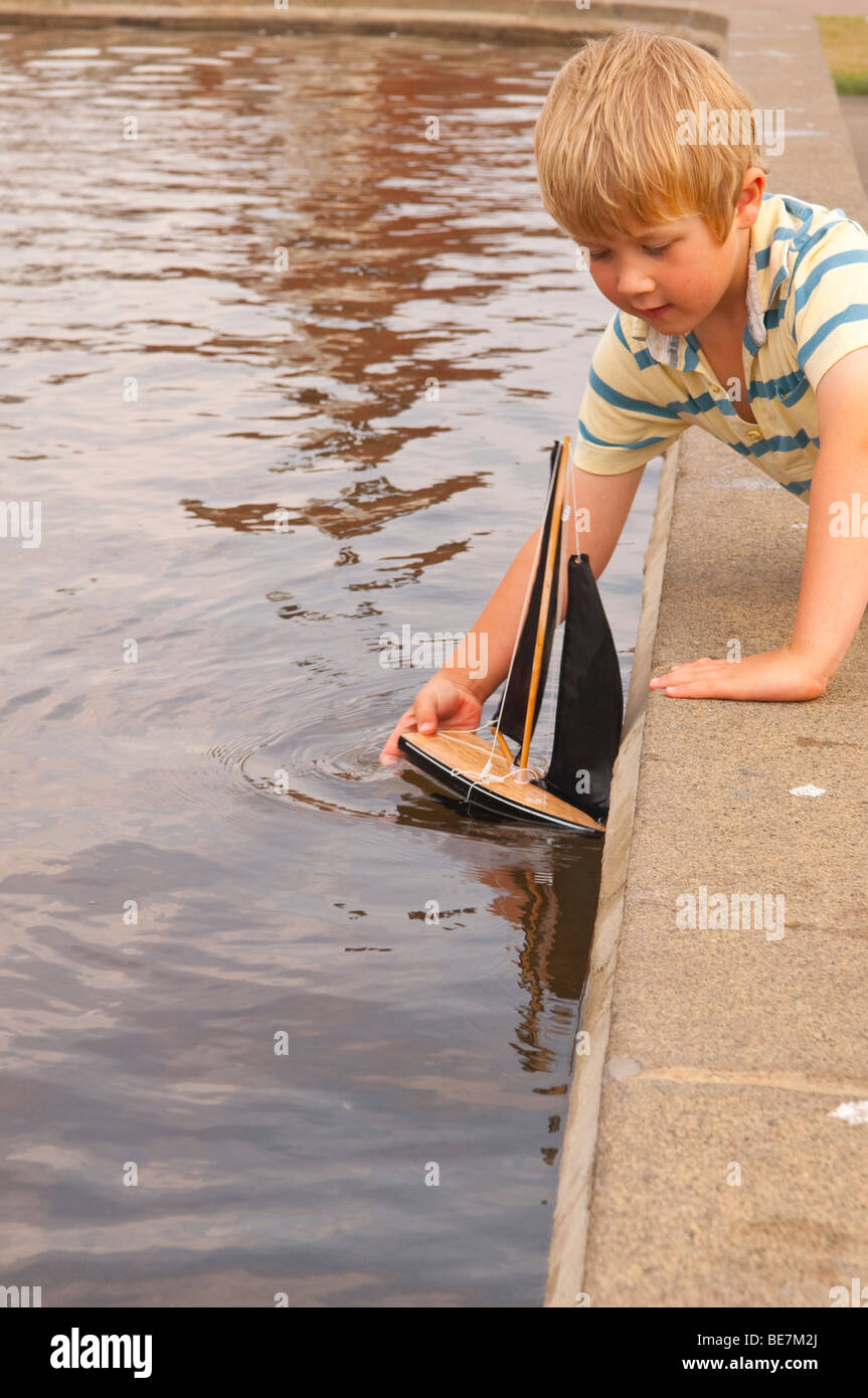 A small boy ( model released ) sailing his toy boat at the boating lake ...