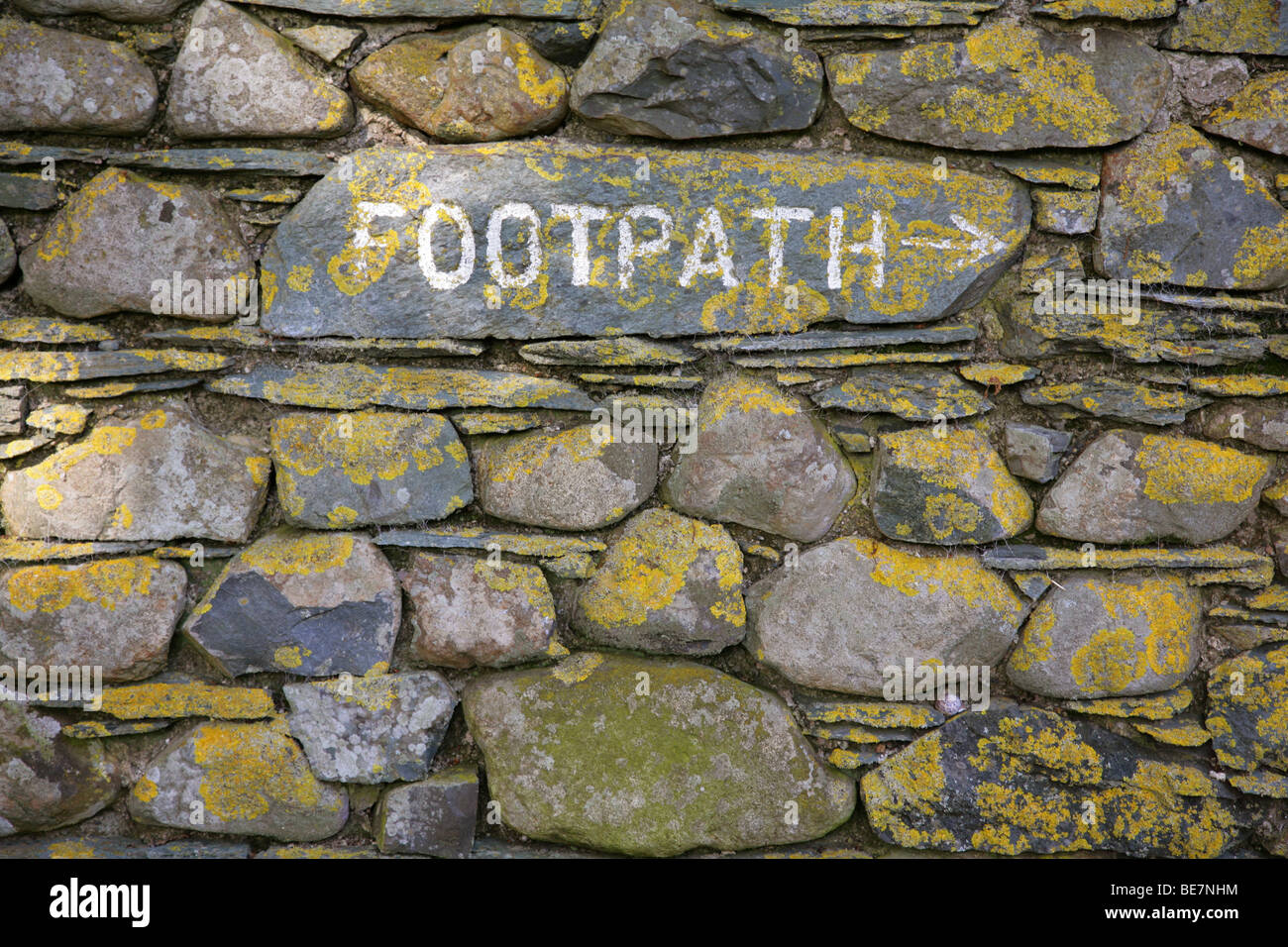 Footpath sign and right-pointing arrow painted onto side of stone wall ...