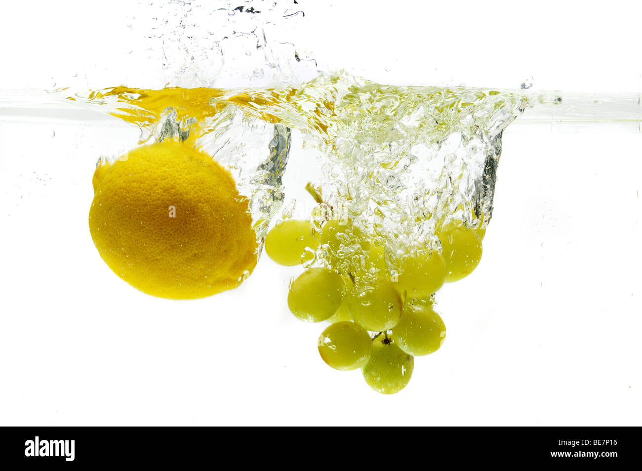 Lemon and grapes dropped in the water isolated against a white ...