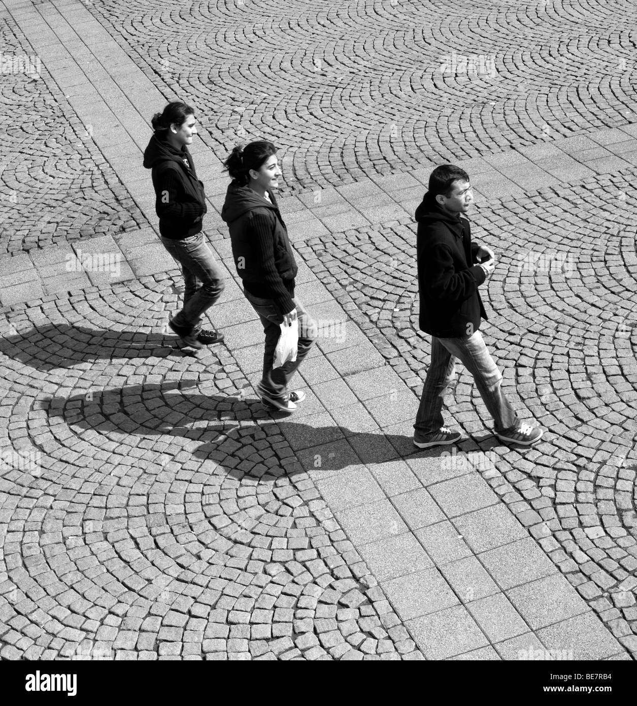 Monochrome of three people walking across cobbled square by Galata ...