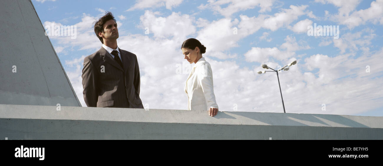 Businessman and businesswoman standing on rooftop, man looking at view ...