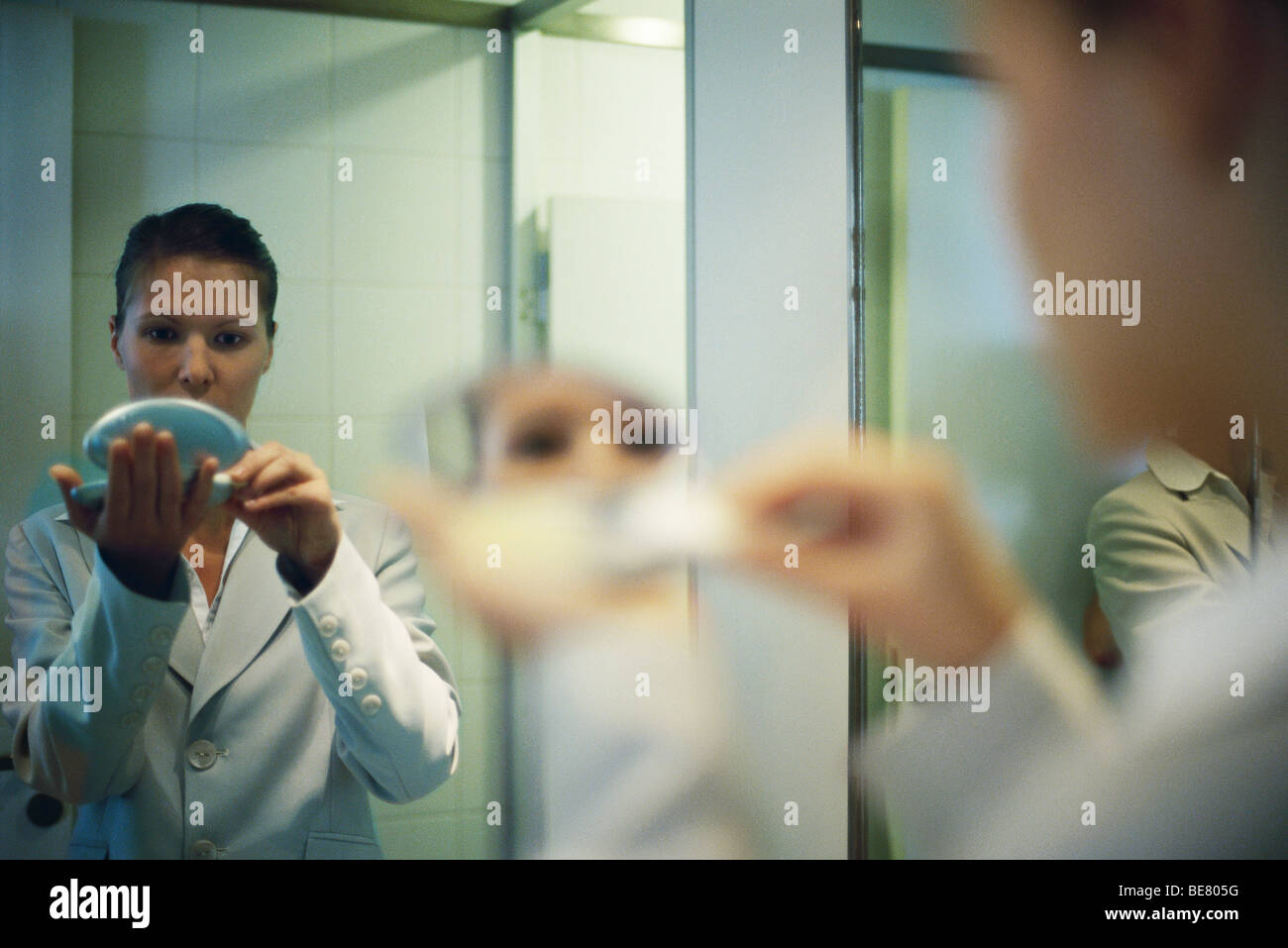 Woman holding powder compact putting on makeup, over shoulder view ...