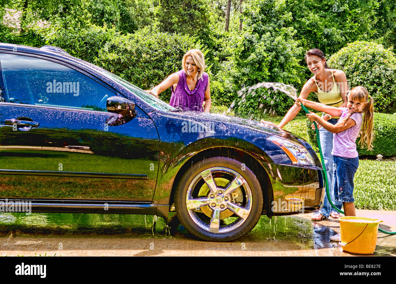 Child and mother and friend having fun at home washiong car together ...