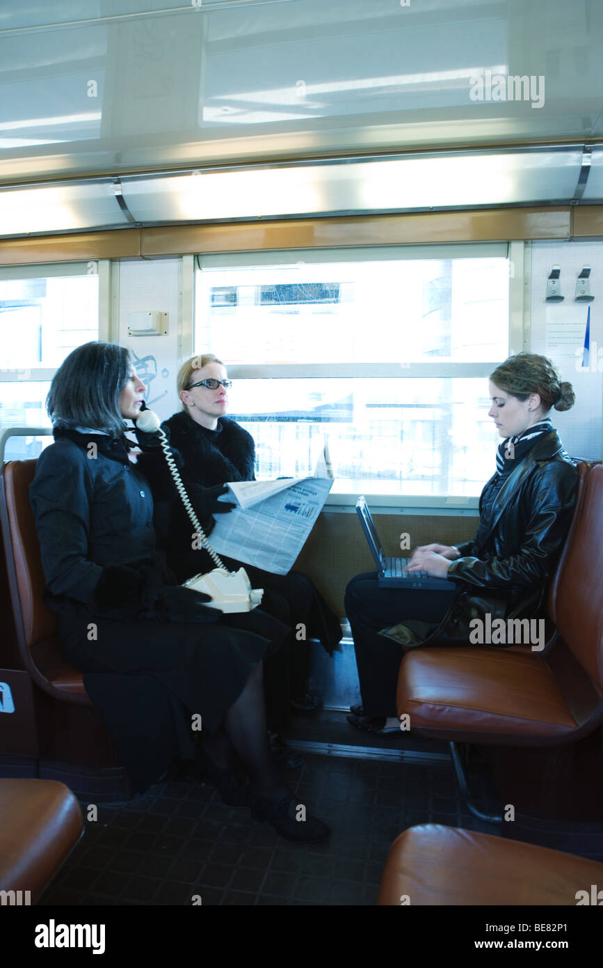 Commuters on train, one using landline phone, another using laptop ...