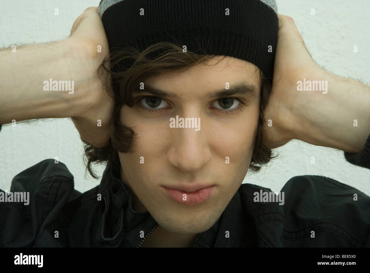 Young man holding hands over ears, staring at camera Stock Photo - Alamy