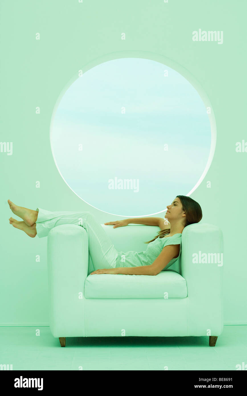 Young woman reclining on armchair, side view Stock Photo - Alamy