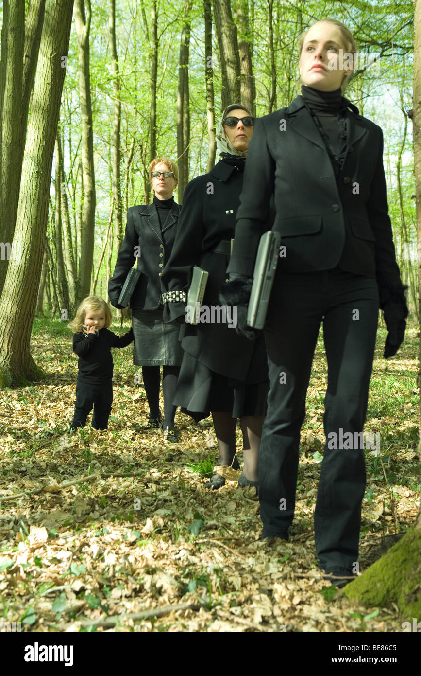 Three women walking in woods, carrying laptop computers, little girl ...
