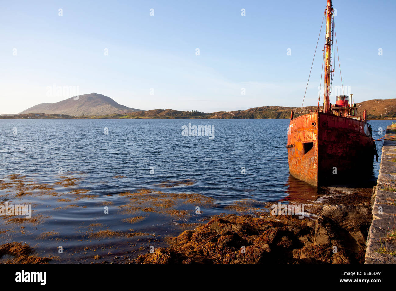 An old rusting ship harboured in a sea inlet in Connemara region of ...