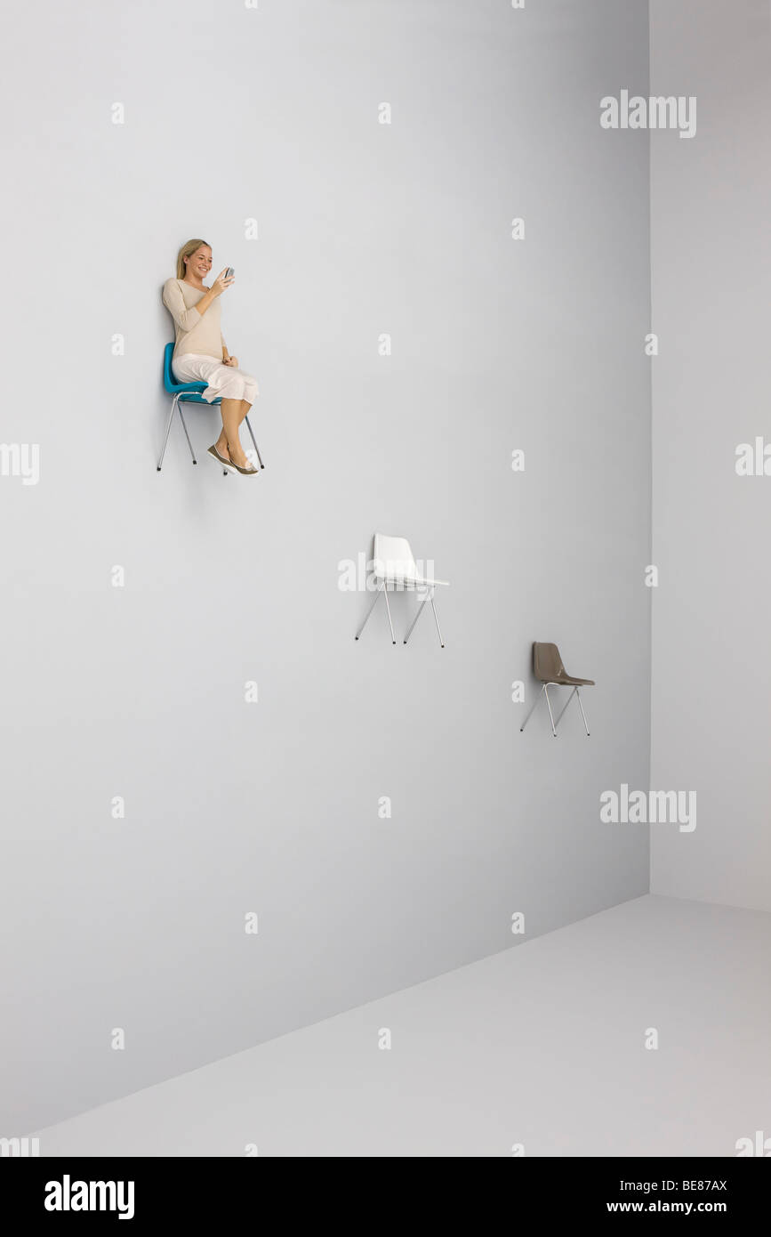 Woman sitting in chair floating in midair, text messaging with cell ...